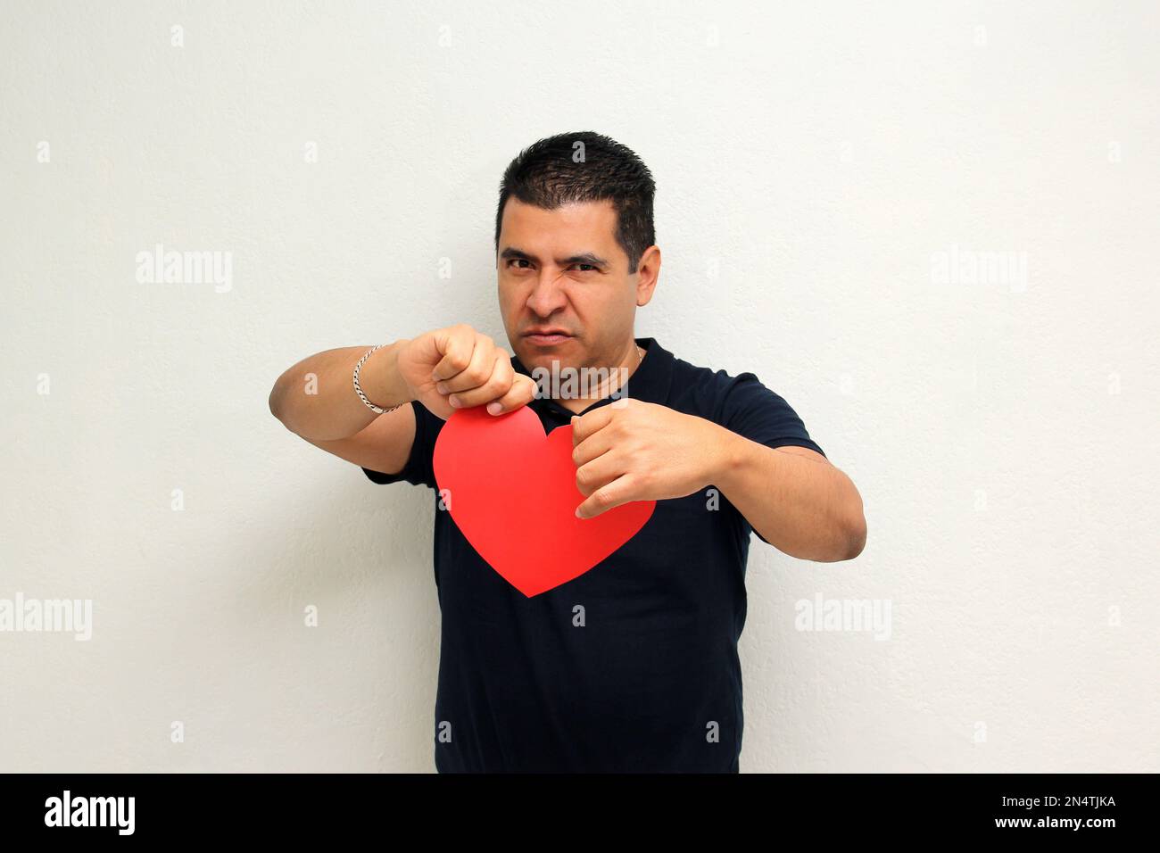 Latino adult man with a big red heart shows his anger, disgust, sadness ...