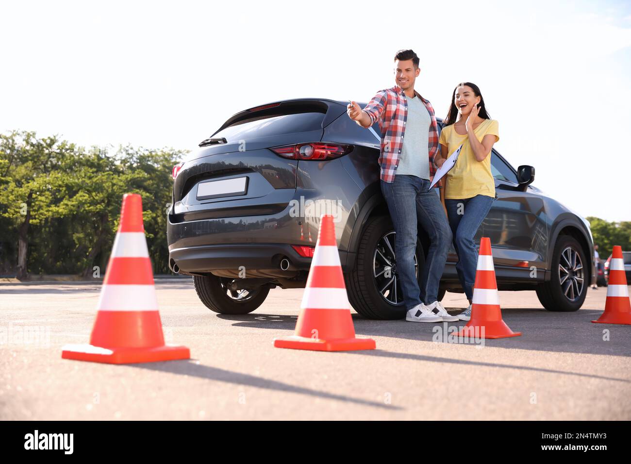 Instructor with clipboard and his student near car outdoors. Driving ...