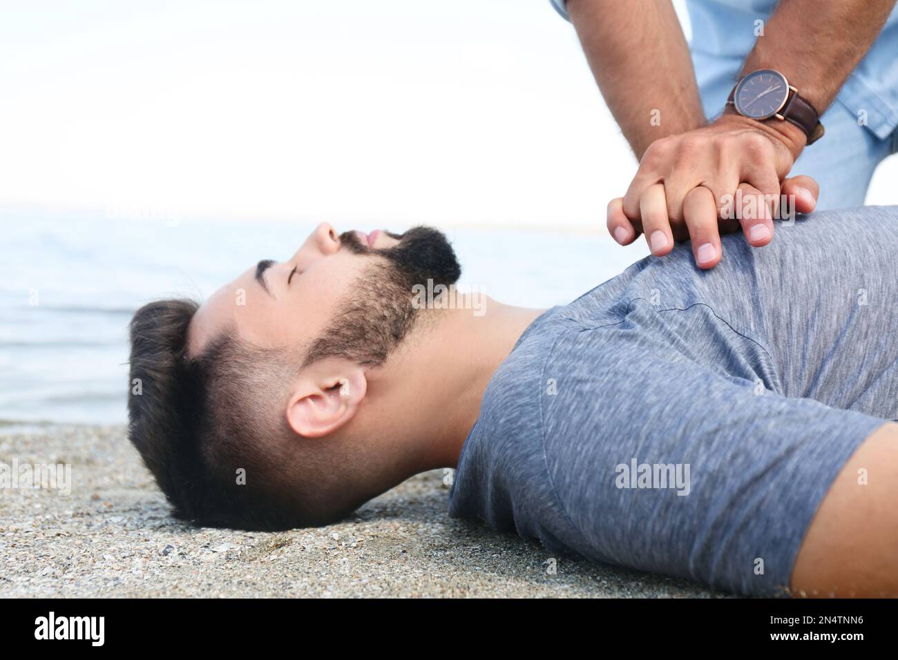 Passerby performing CPR on unconscious young man near sea. First aid ...