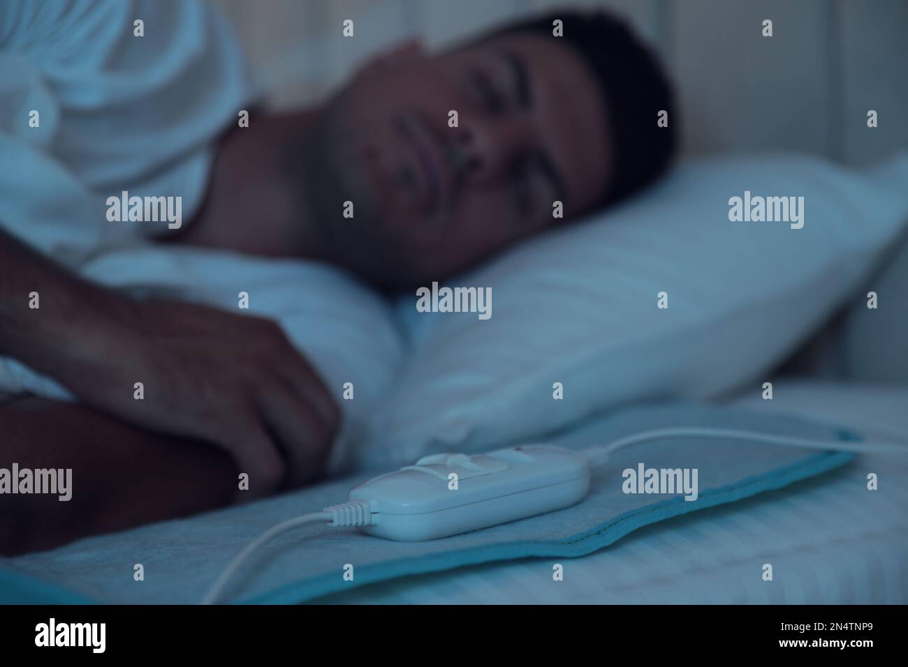 Man sleeping in bed with electric heating pad, focus on cable Stock ...
