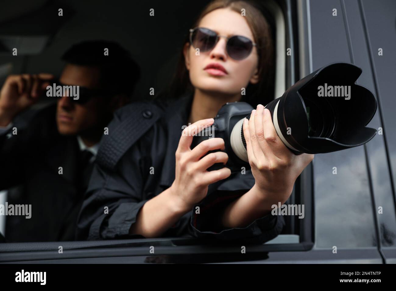 Private detectives with modern camera spying from car, focus on lens ...