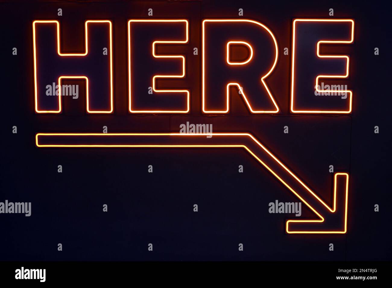 Illuminated sign saying: 'Here' with an arrow underneath to point ...