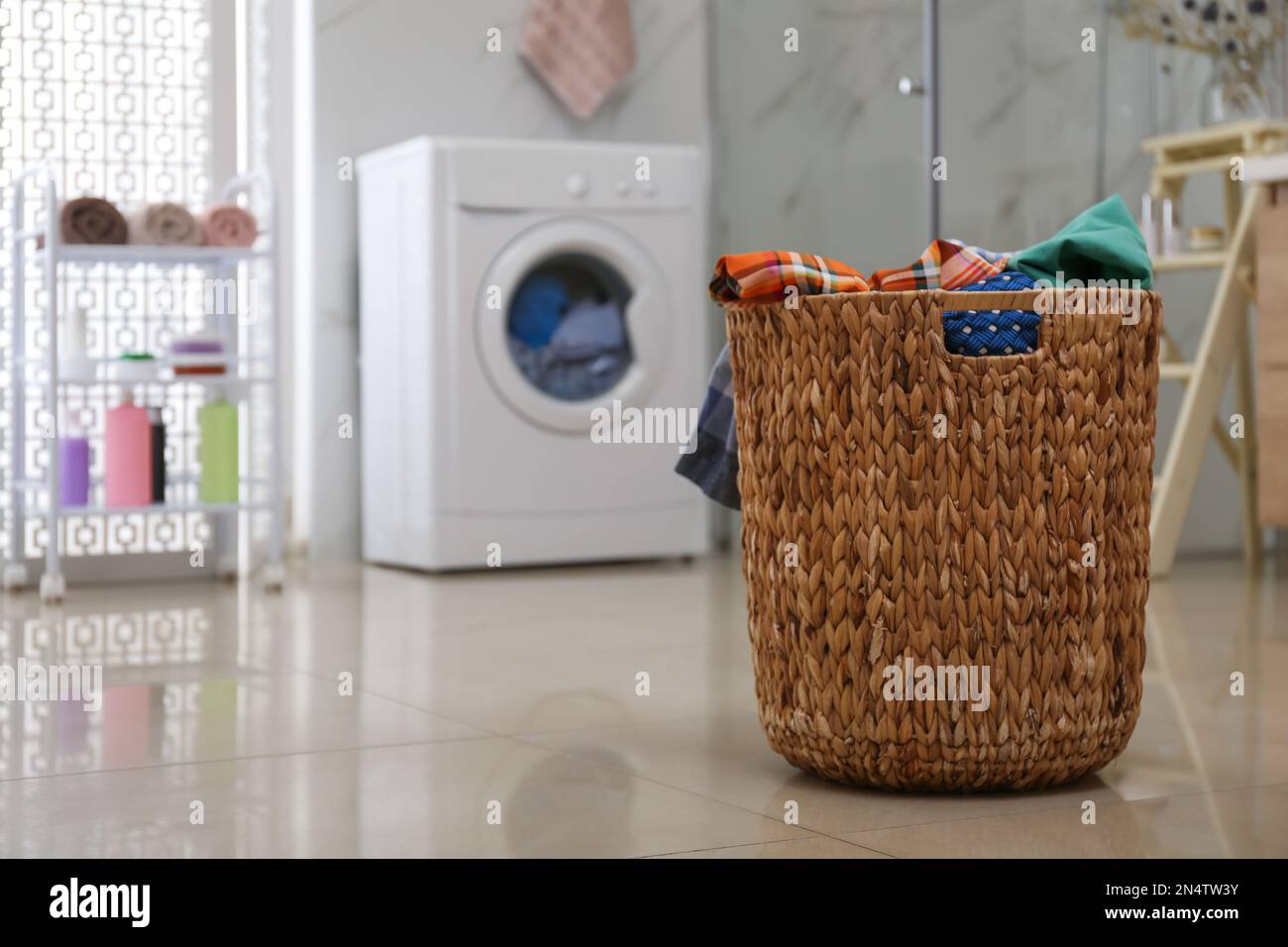 Wicker laundry basket full of different clothes on floor in bathroom ...