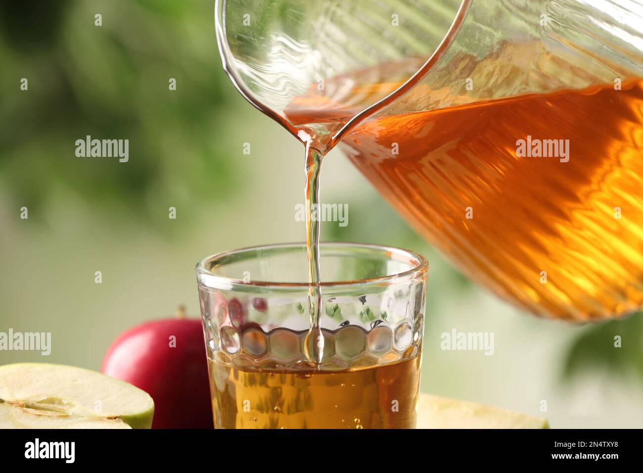 Pouring apple juice into glass on blurred green background, closeup ...