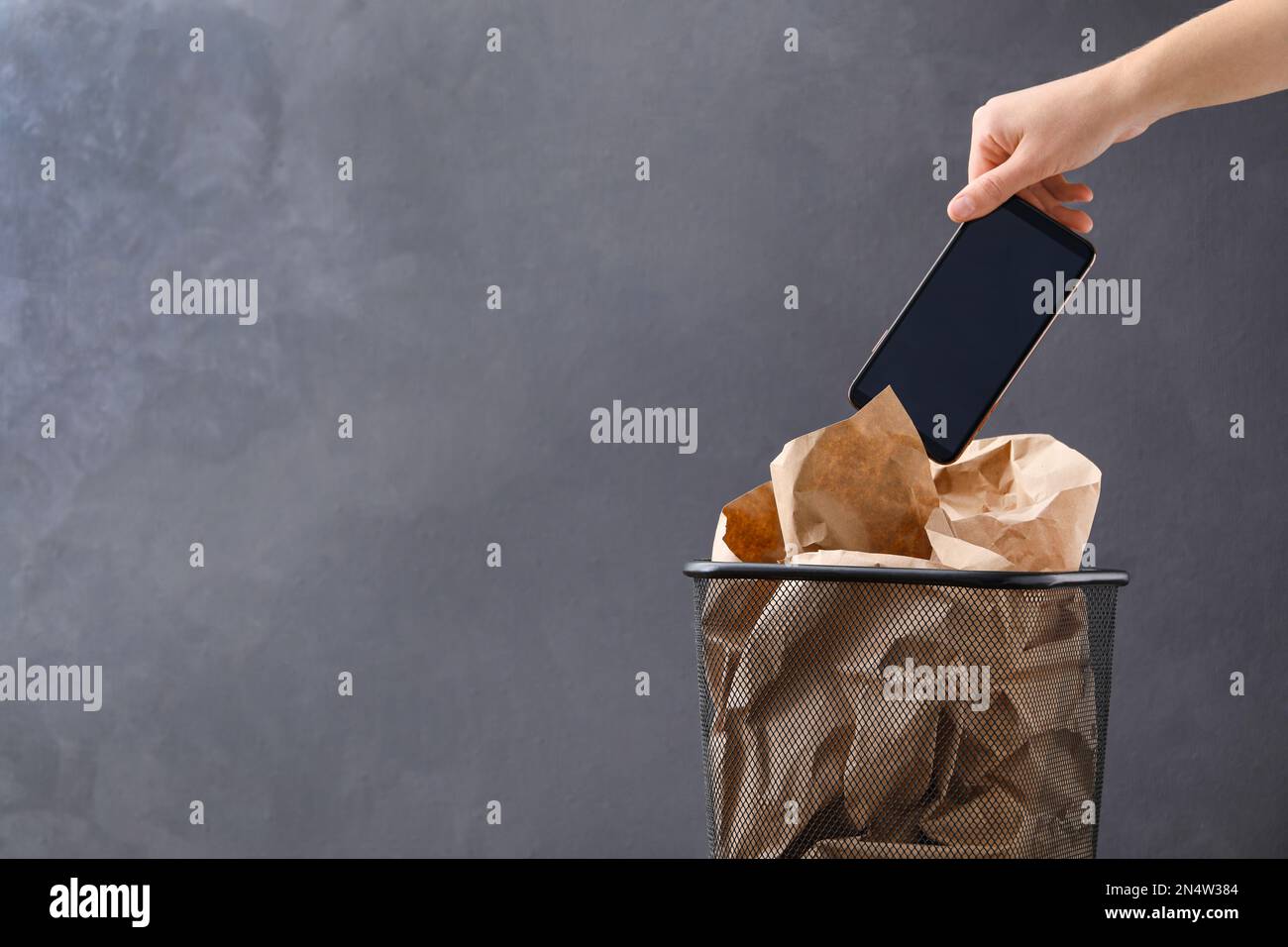 Closeup view of woman throwing smartphone into trash bin on grey ...