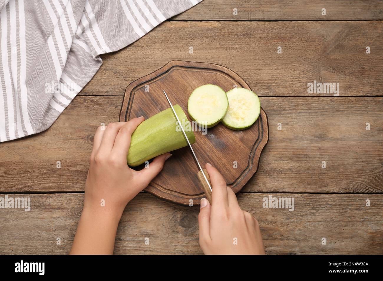 Woman cutting zucchini at wooden table, top view Stock Photo - Alamy