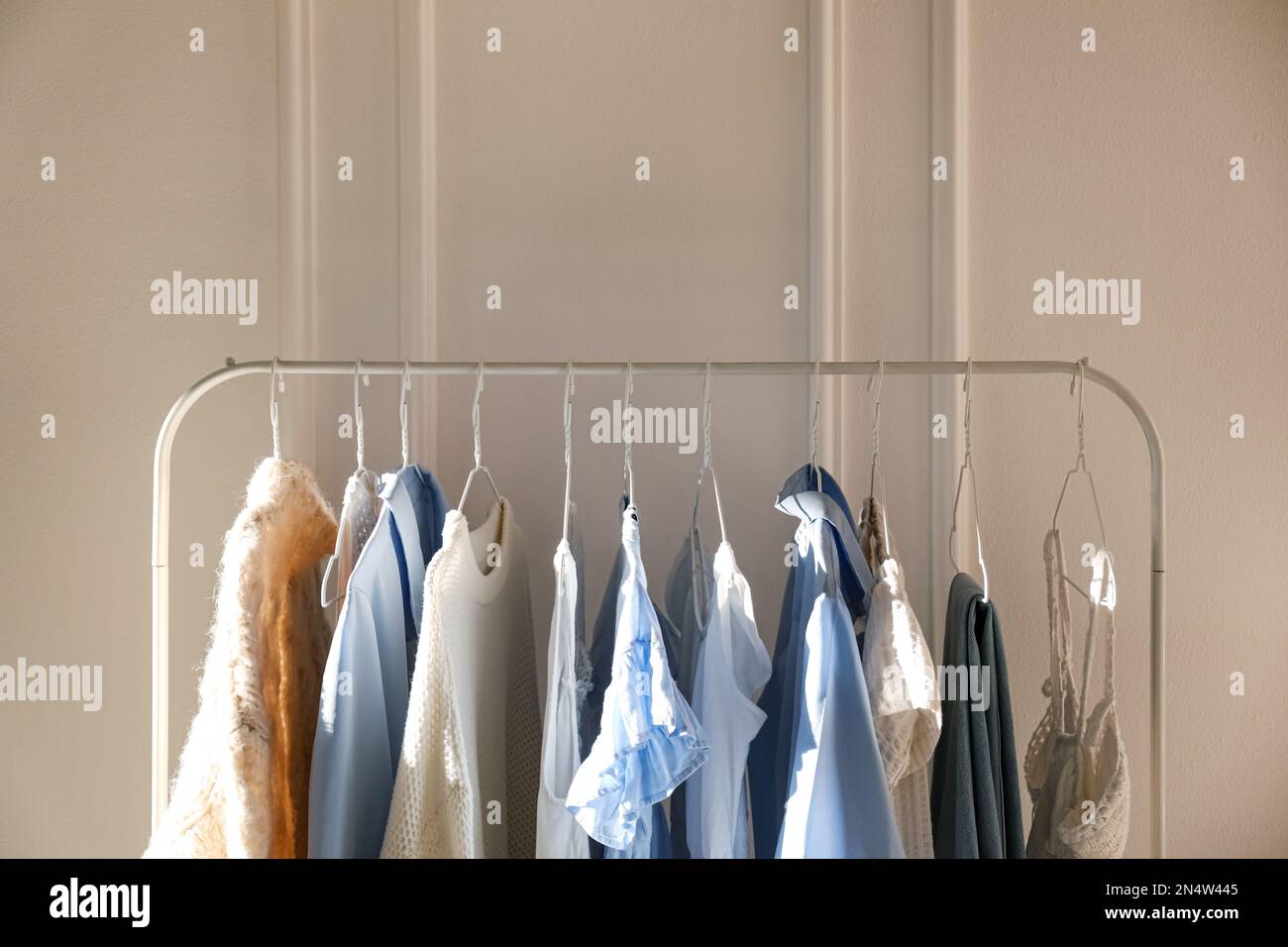 Rack with stylish women's clothes near white wall. Interior design ...