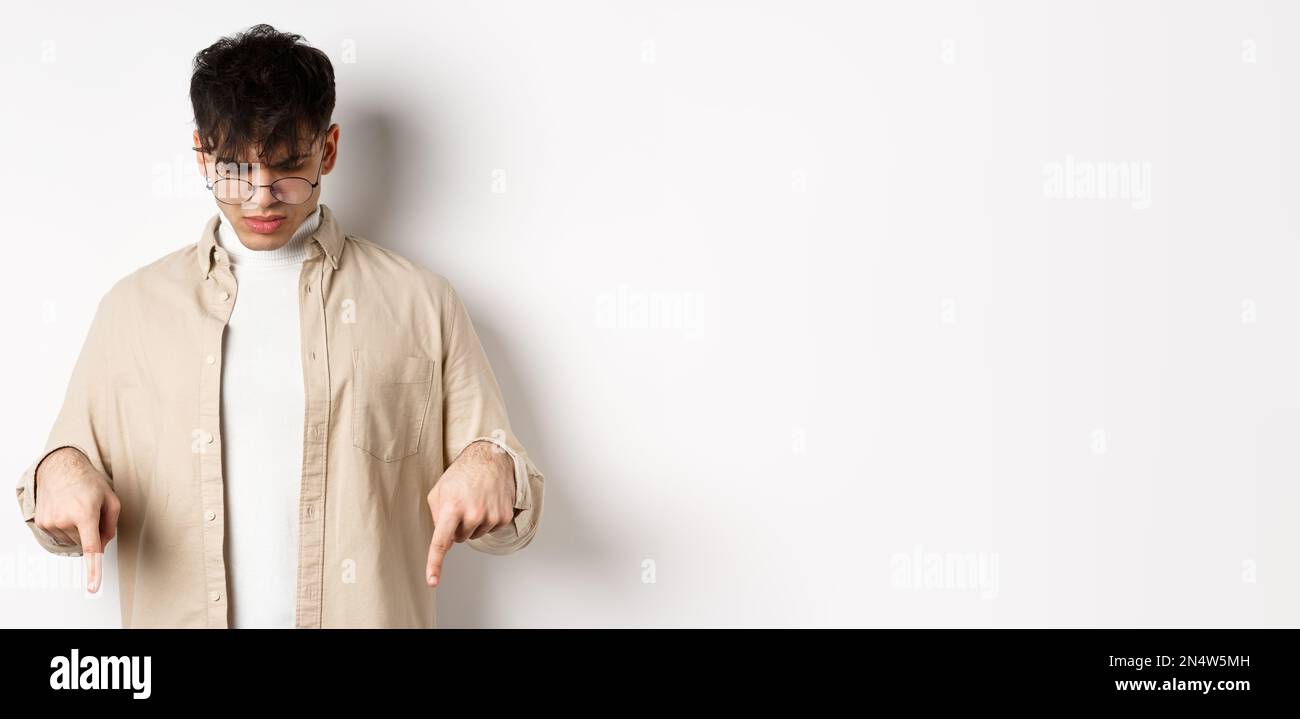 Confused frowning guy in glasses looking, pointing fingers down at ...