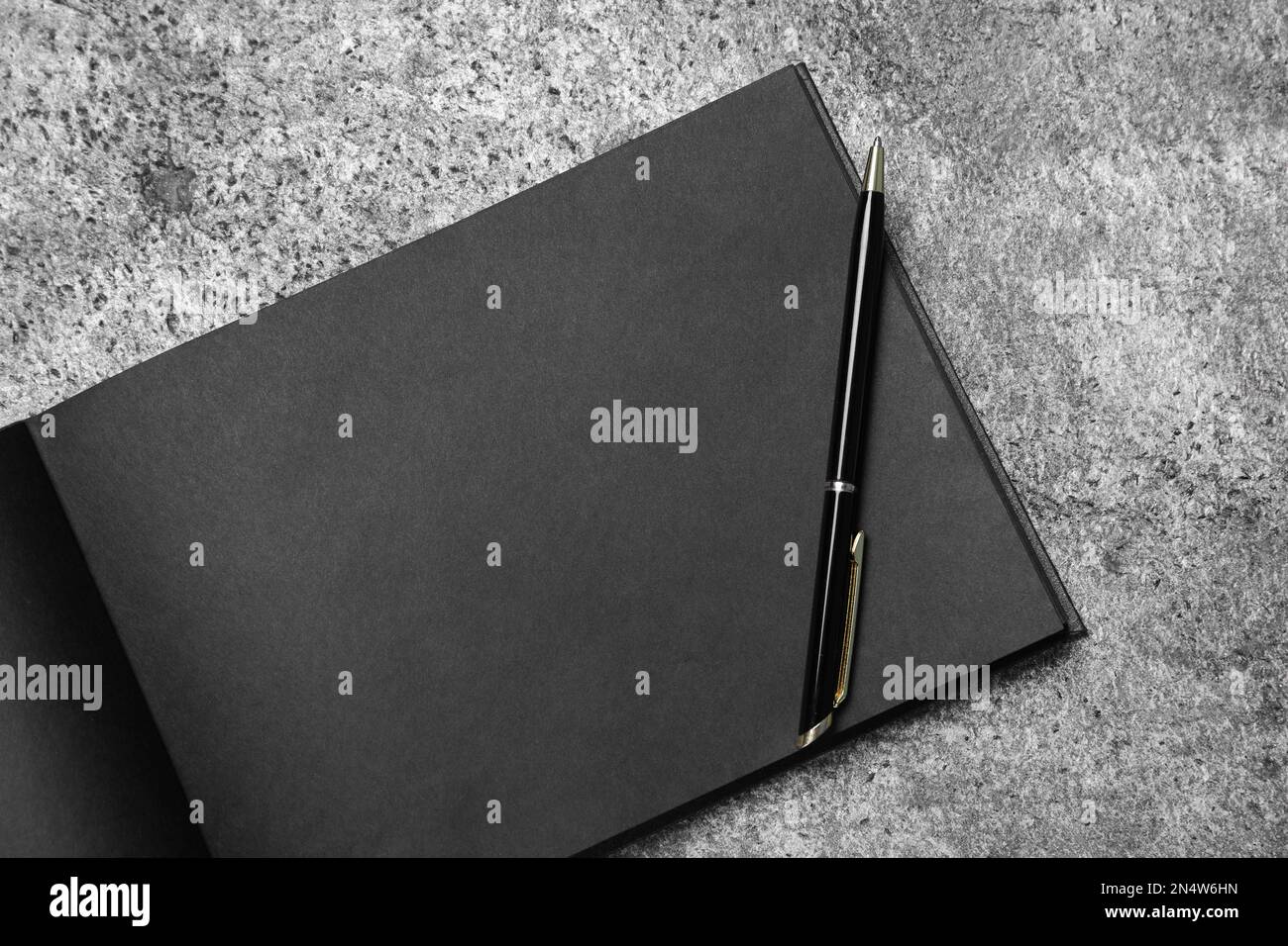 Open sketchbook with black pages and pen on grey stone table, top view ...