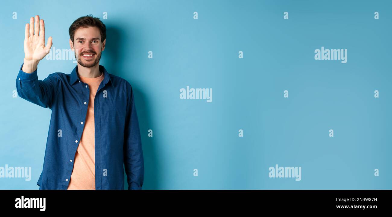 Friendly young man smiling and raising hand up for high five, waiving ...
