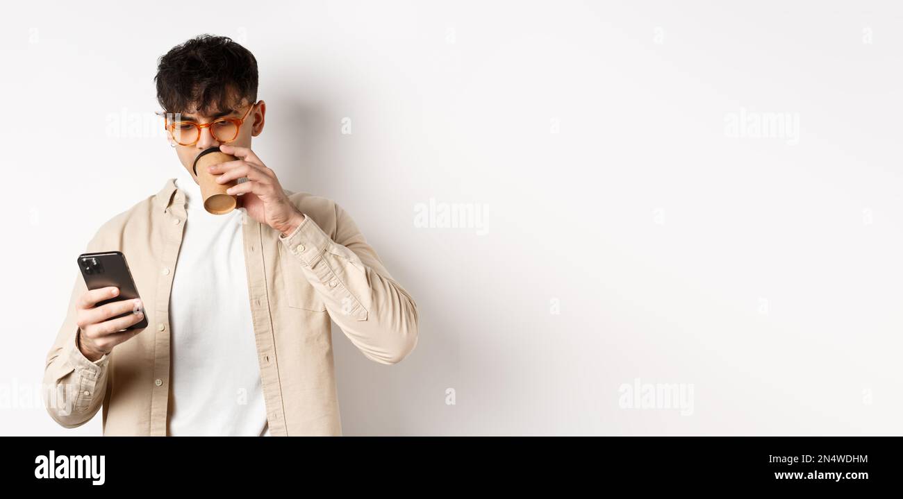 Real people. Young man reading smartphone screen and drinking coffee ...