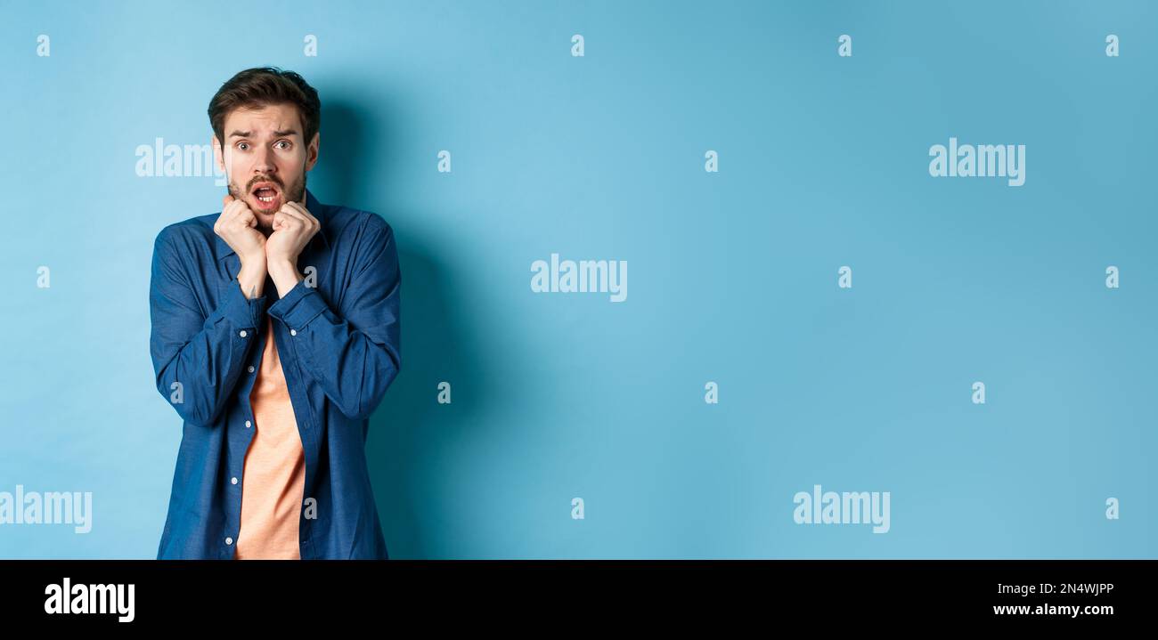 Scared young man gasping and screaming frightened, looking terrified at something, standing on ...