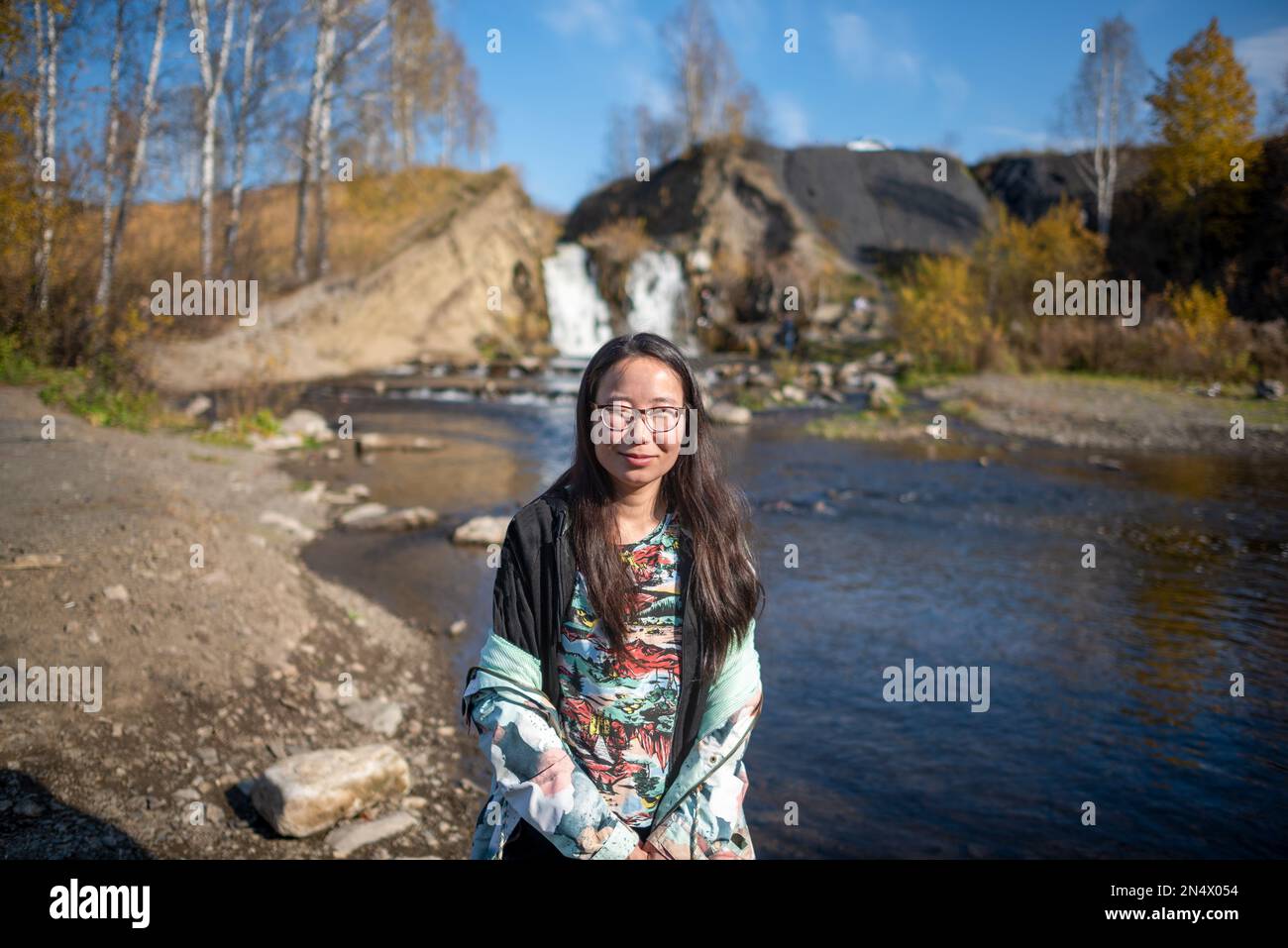 Yakut Asian Girl In Glasses Posing Smiling On The Background Of A Small Waterfall In The Fall