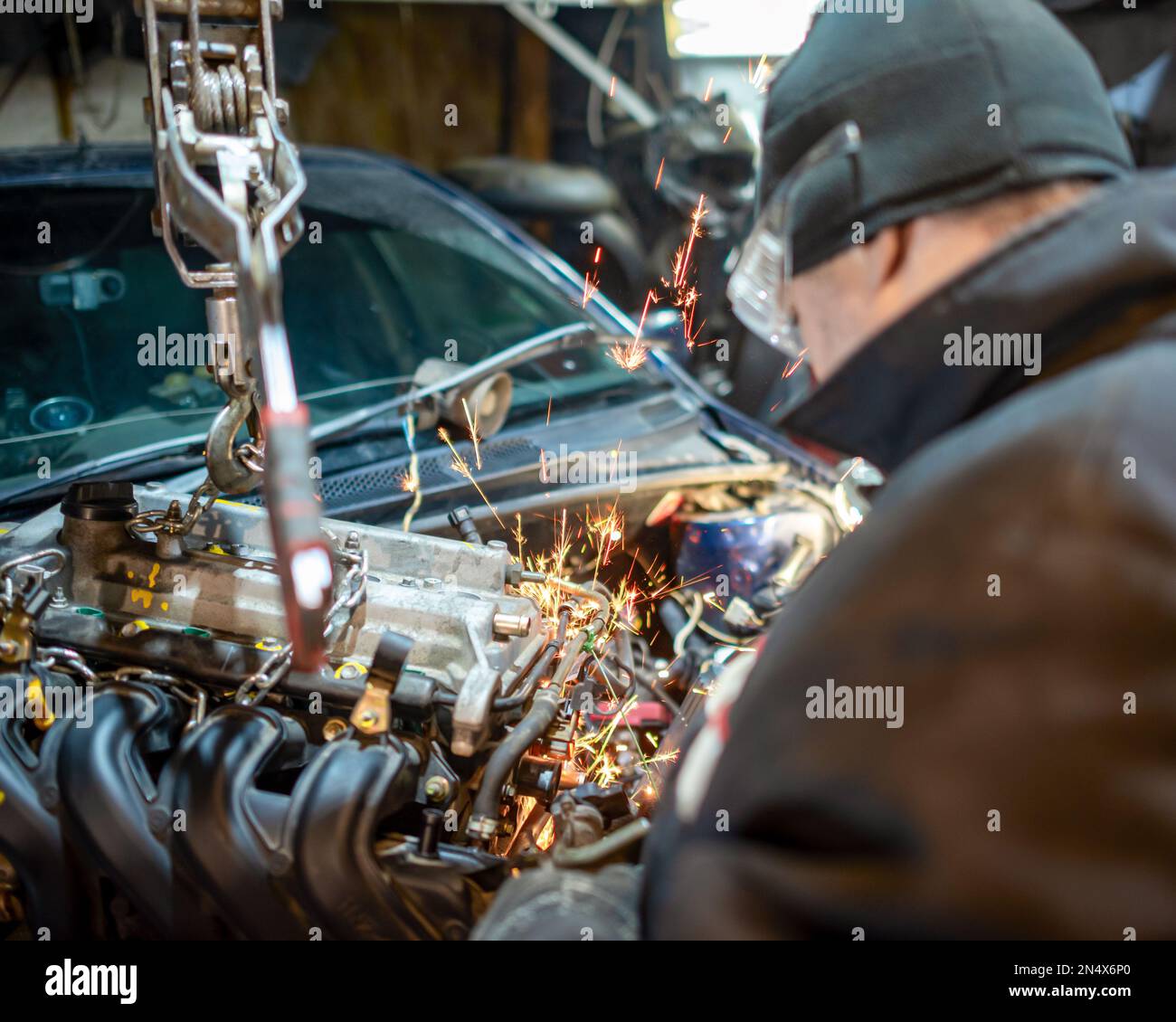 A bespectacled car mechanic in the garage works with sparks flying from ...