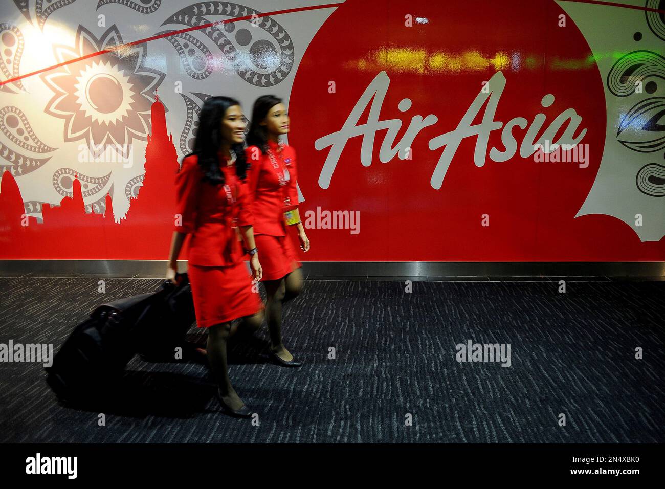 AirAsia employees walk along the wall painted with a giant logo of the ...
