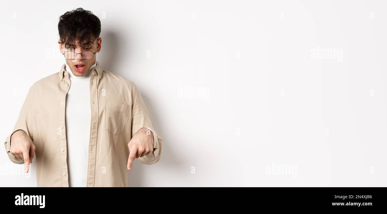 Amazed young guy in glasses look and point down, open mouth and say wow ...