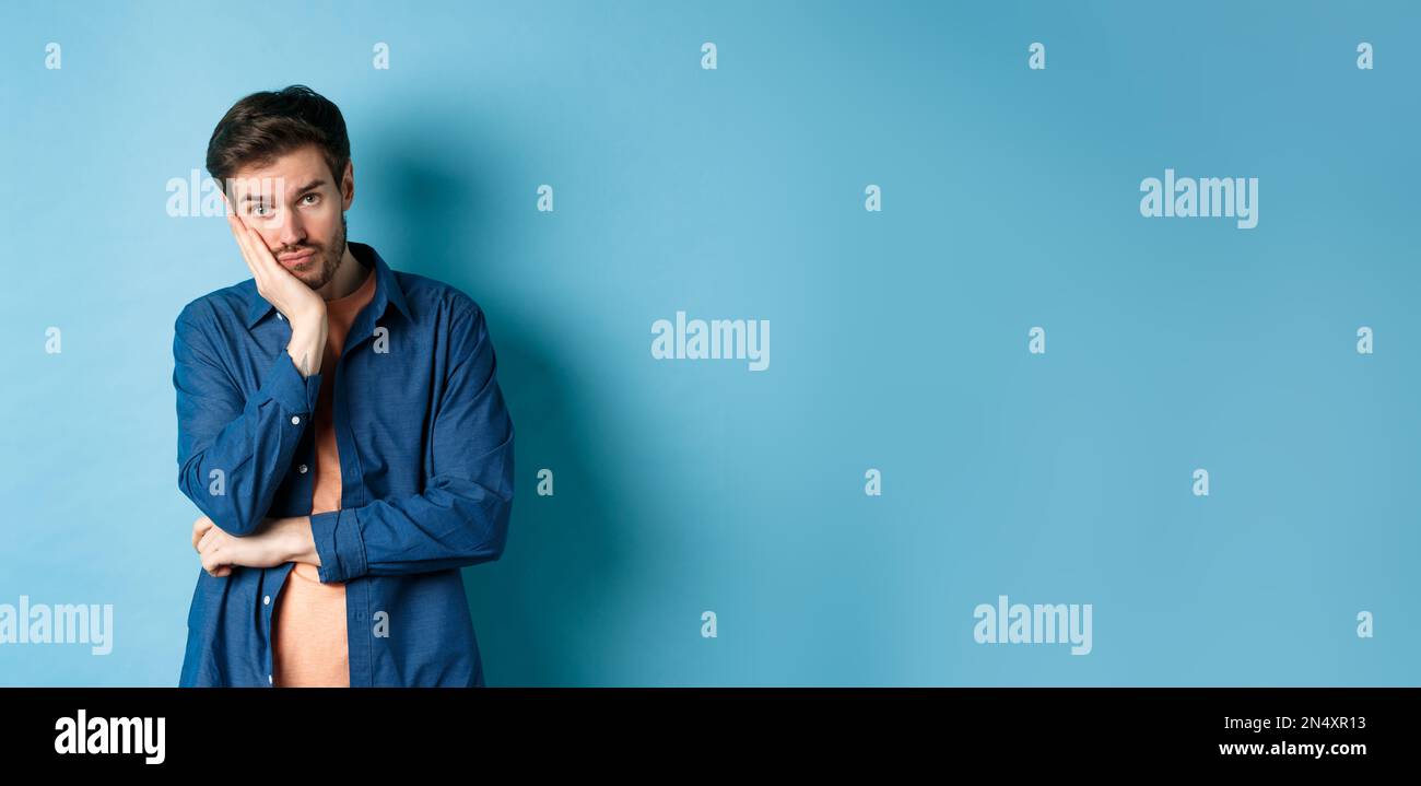 Sad and bored man lean face on hand, looking at camera empty-headed ...