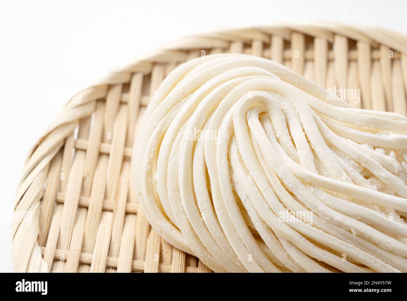 Fresh udon noodles in a bamboo colander placed on a white background ...