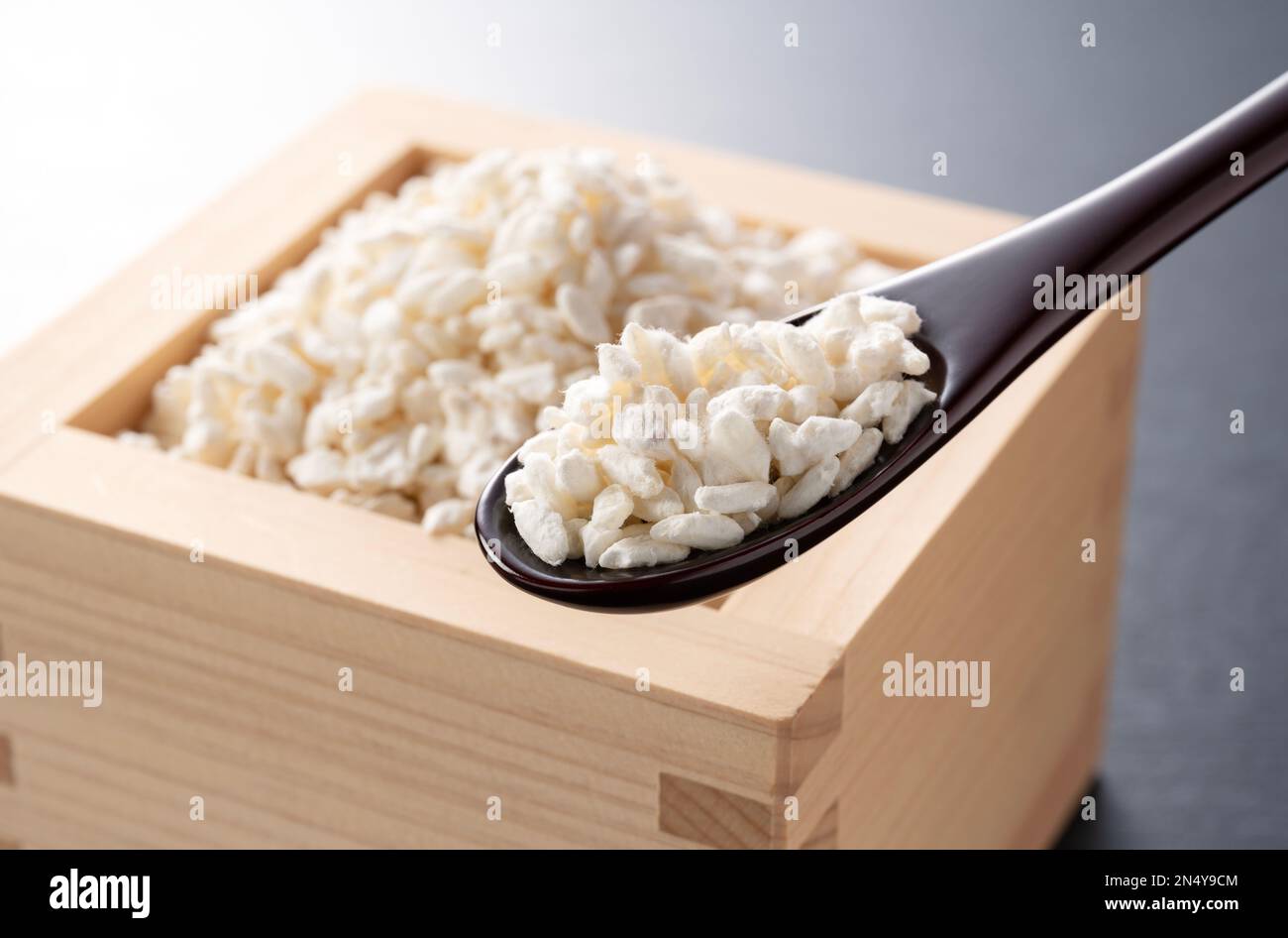 Rice koji in a box and a wooden spoon placed against a black background ...