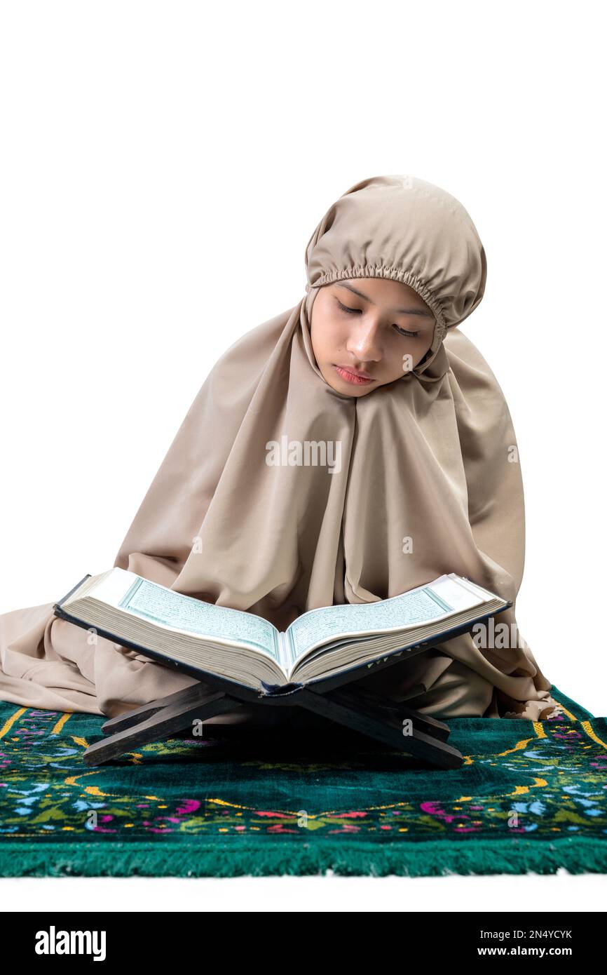 Asian Muslim girl in hijab on prayer rug reading the Quran isolated ...