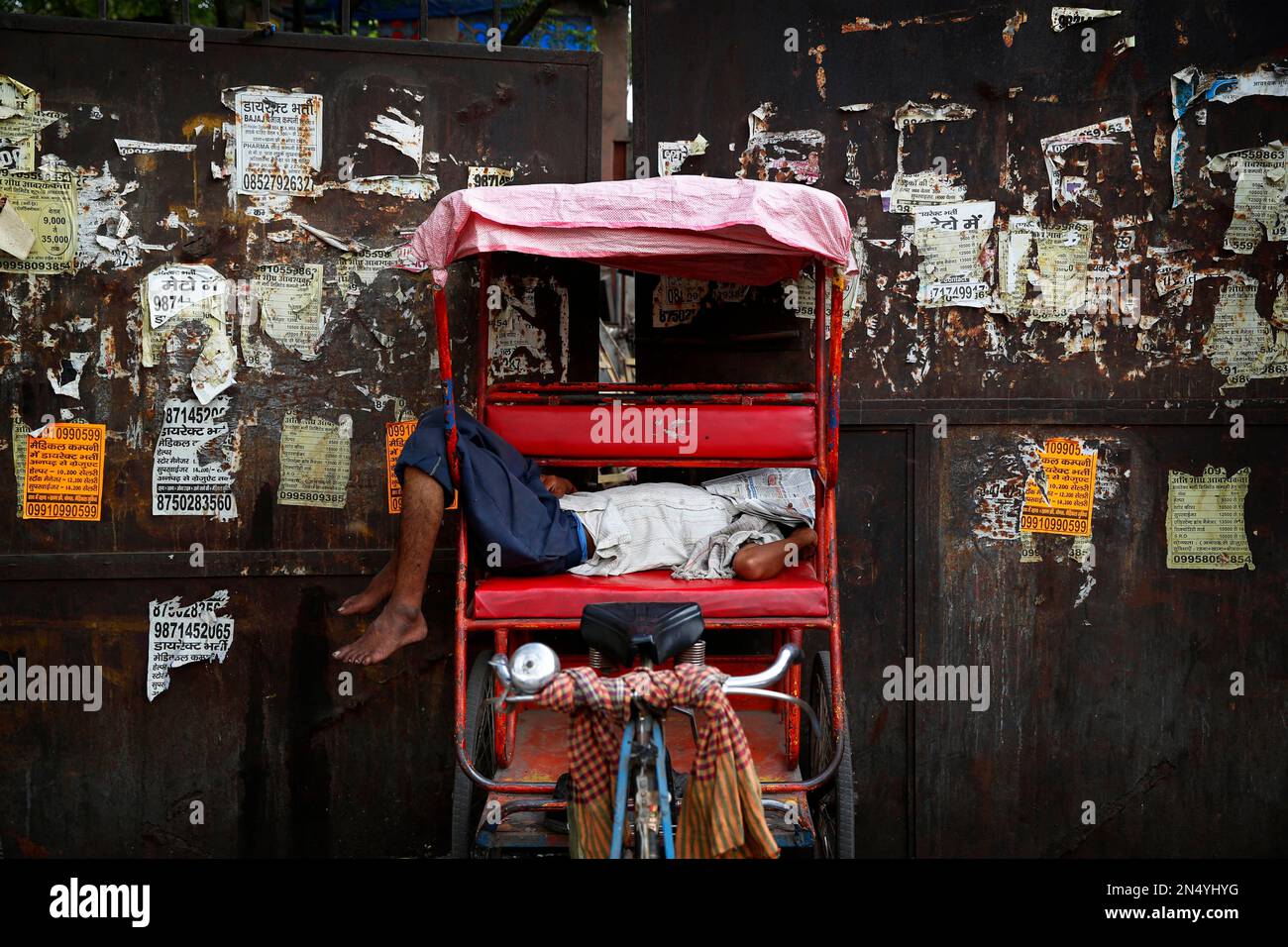 A rickshaw puller covers his face with a newspaper as he takes a nap in a hot summer afternoon ...