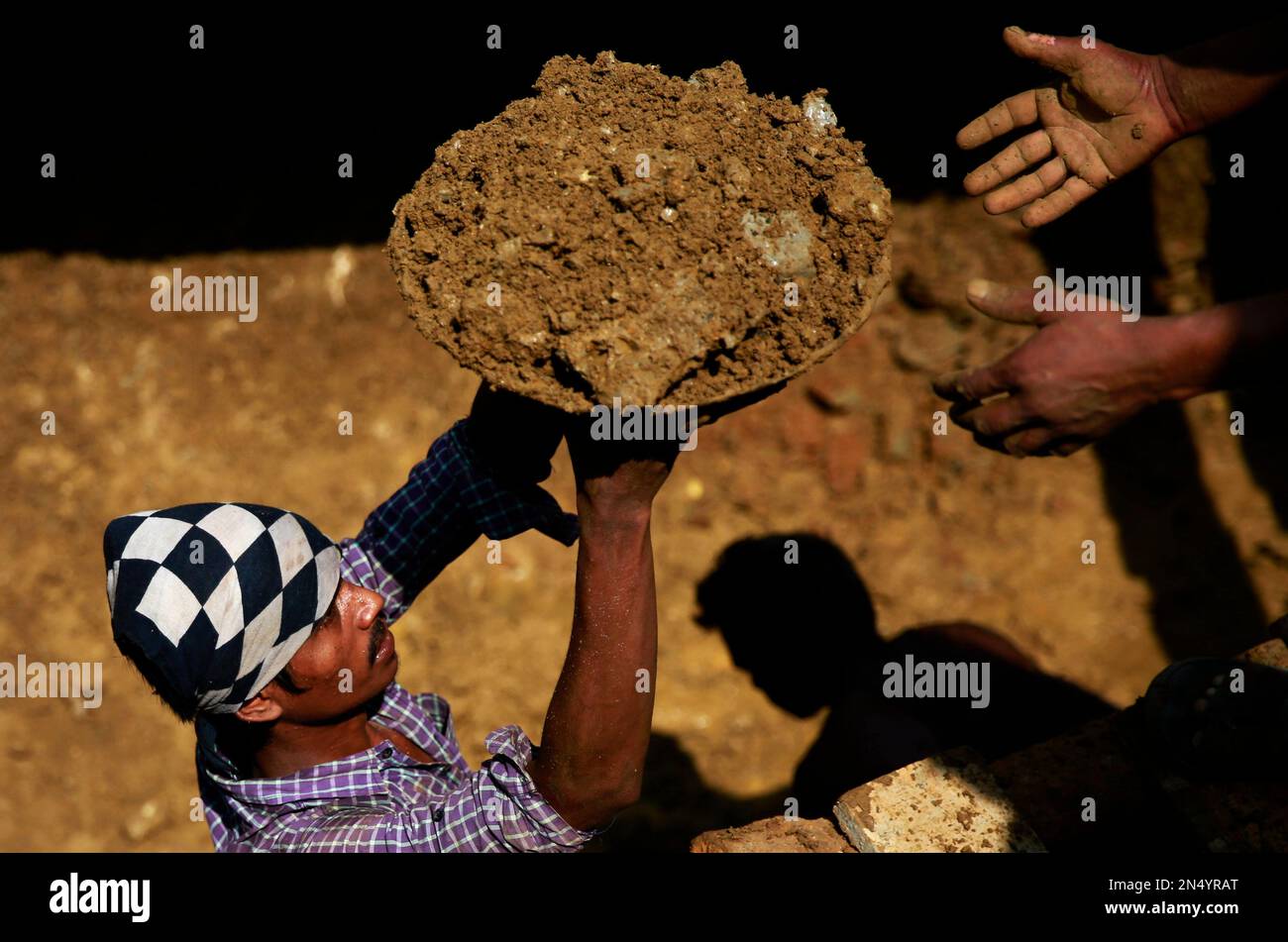 An Indian laborer passes on a tray filled with gravel to another as ...