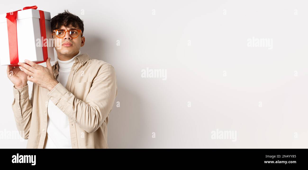 Intrigued guy listening whats inside gift box, trying guess present ...