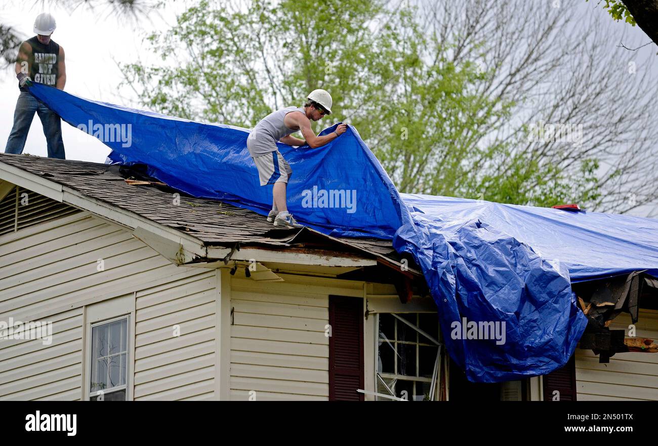 Bret Gullick, left, and Alec Reed place a tarp over the roof of a home ...