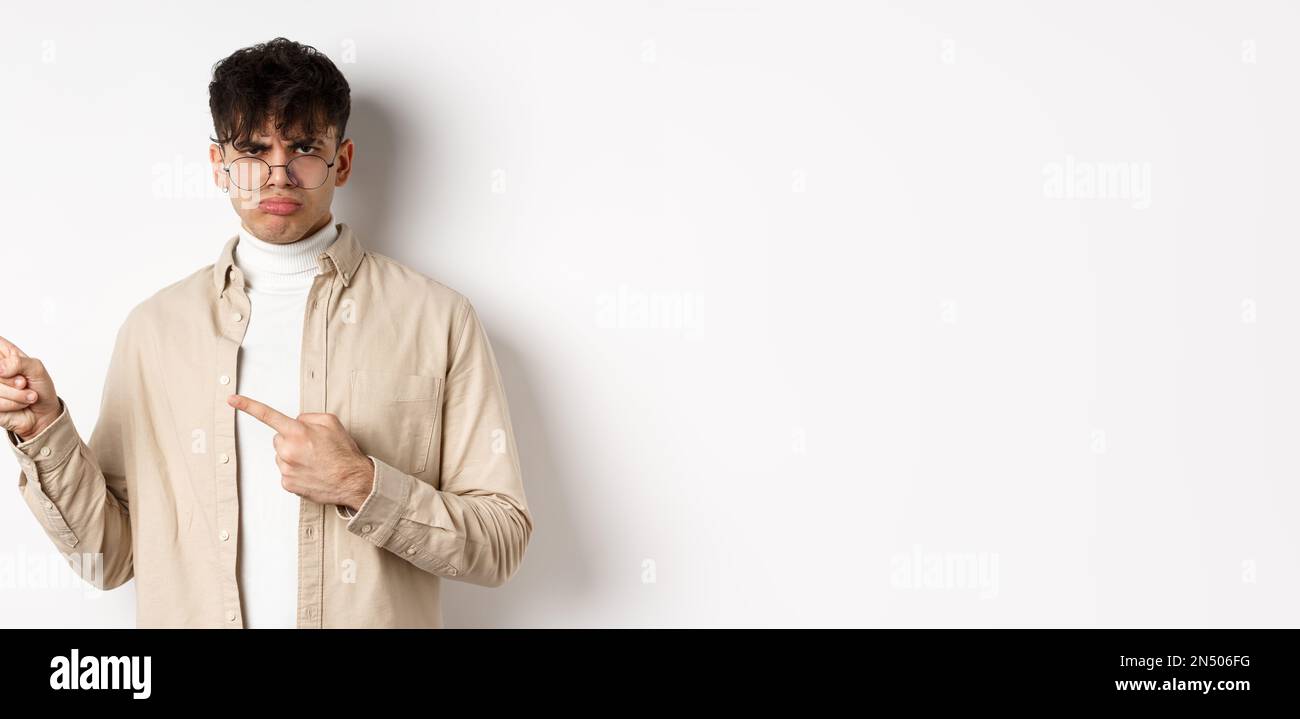 Sad and grumpy boy pointing fingers left, sulking with childish ...