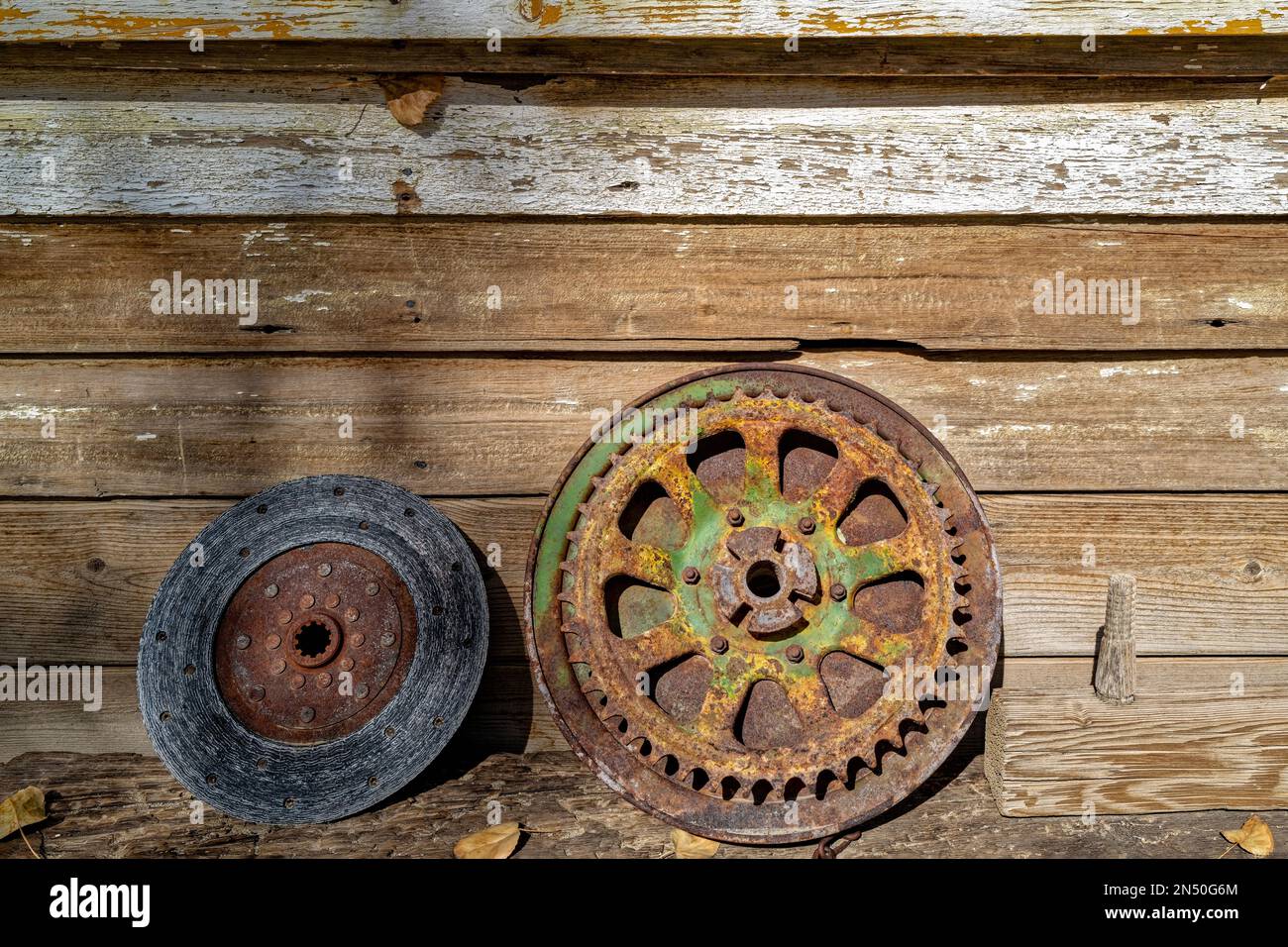 A rusty gear and brake rotor leaning against the wall of an old wooden ...