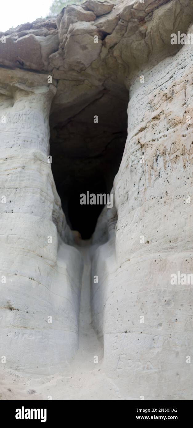 A cave in a clay gorge with overhanging rocks and darkness far away in ...