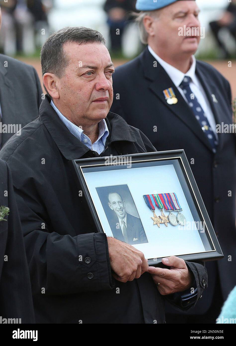 A man holding a memorial photo framed with war medals marches past the ...