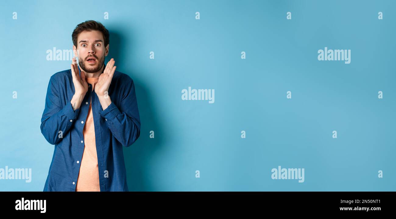 Shocked and scared young man standing in stupor, raising hands up and ...