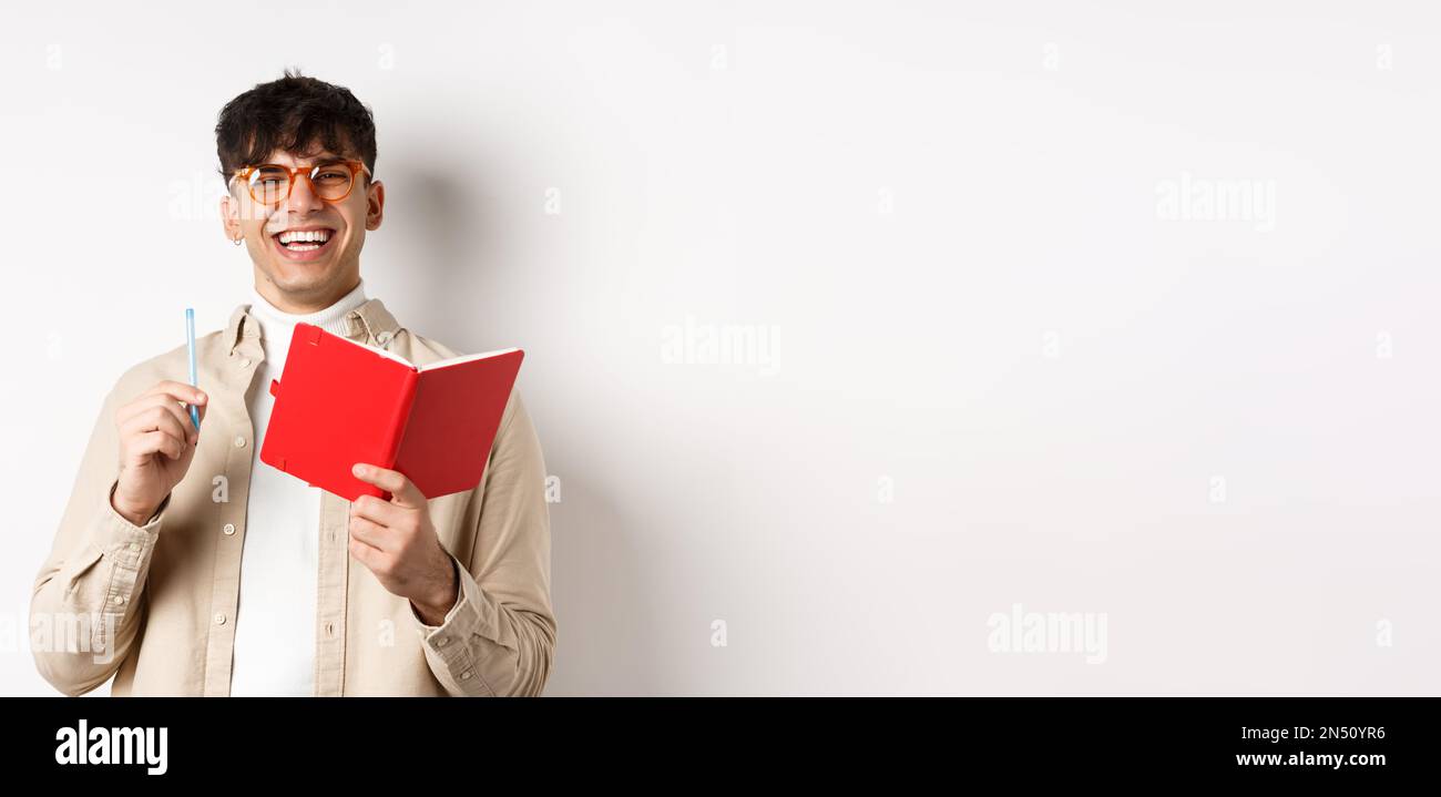 Cheerful young man in glasses laughing and taking notes, writing down ...