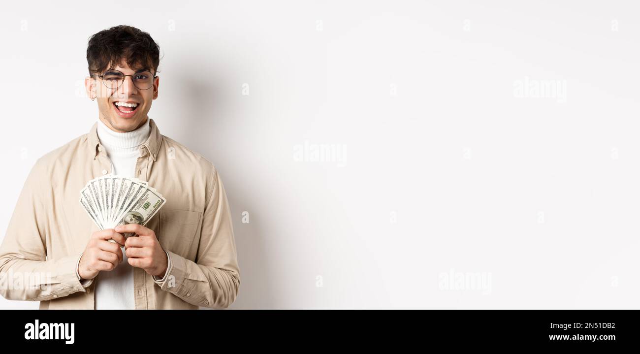 Handsome young man winking and showing dollar bills, holding fan of ...
