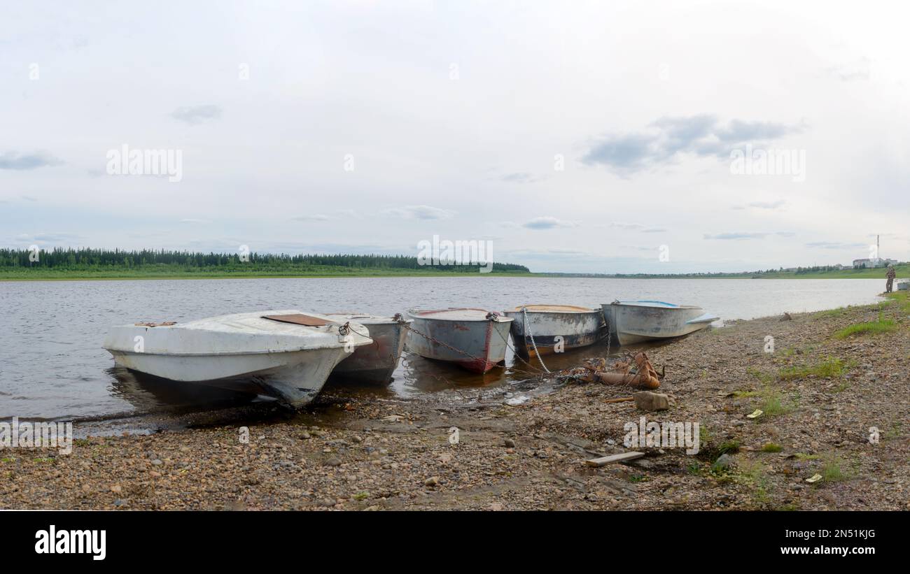 Five old metal boats are tethered near the shore against the background ...