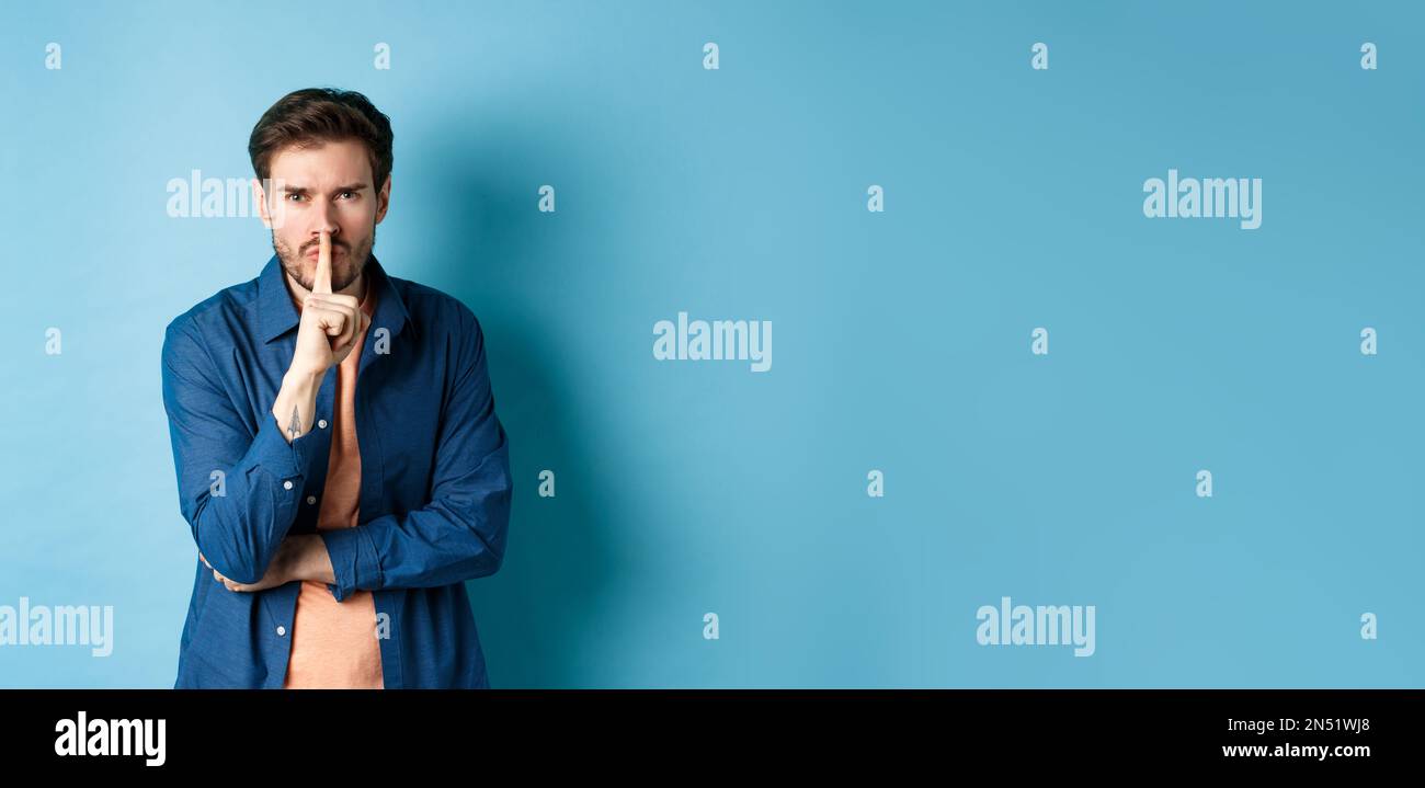 Angry man shushing, press finger to lips and frowning, tell to be quiet ...