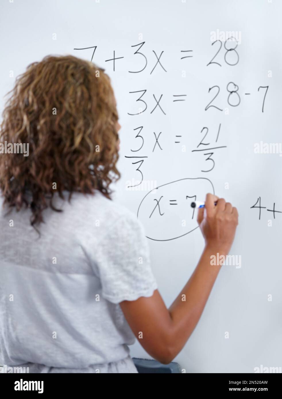 Maths class. A young teacher doing maths equations on the whiteboard ...