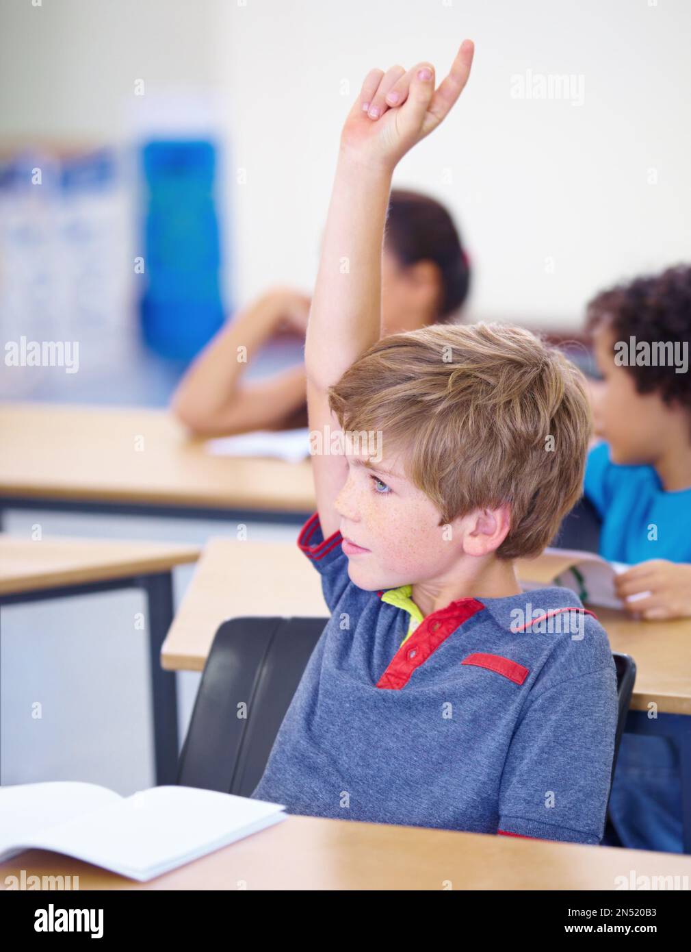 Hes got the answer. A young boy holding his hand up in class to answer ...