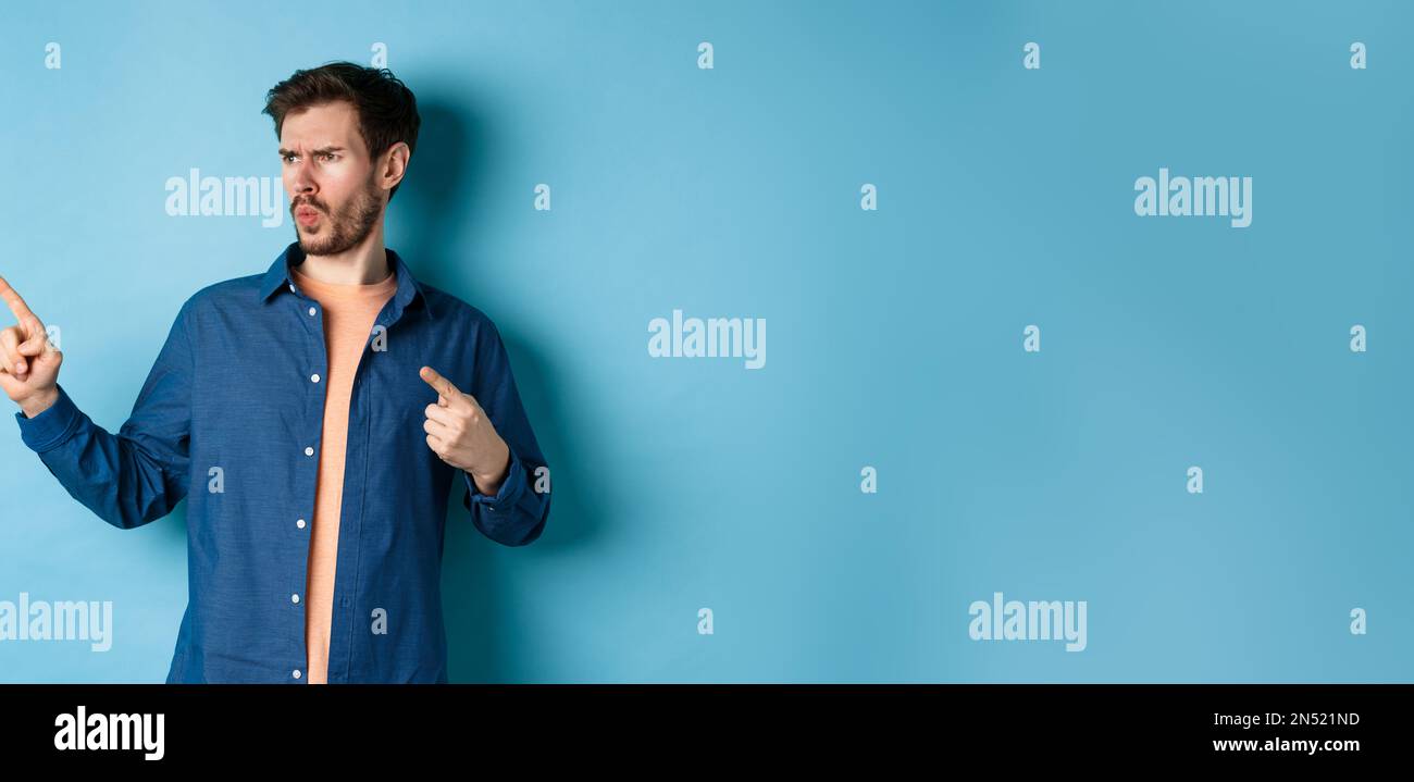 Confused and annoyed guy pointing and looking left at empty space with ...