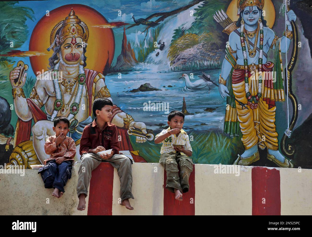 Children eat sacred food "Prasadam" in front of a temple wall with a ...