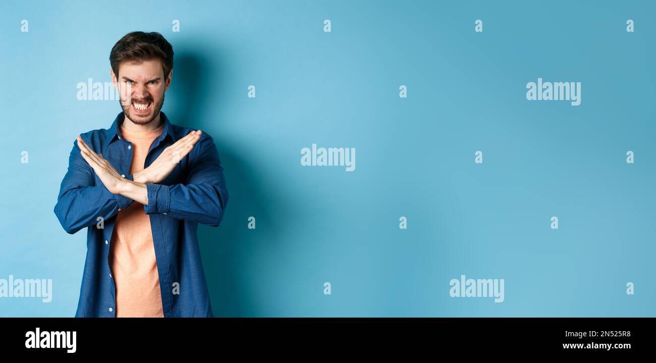 Angry young man frowning and clenching teeth outraged, showing cross ...