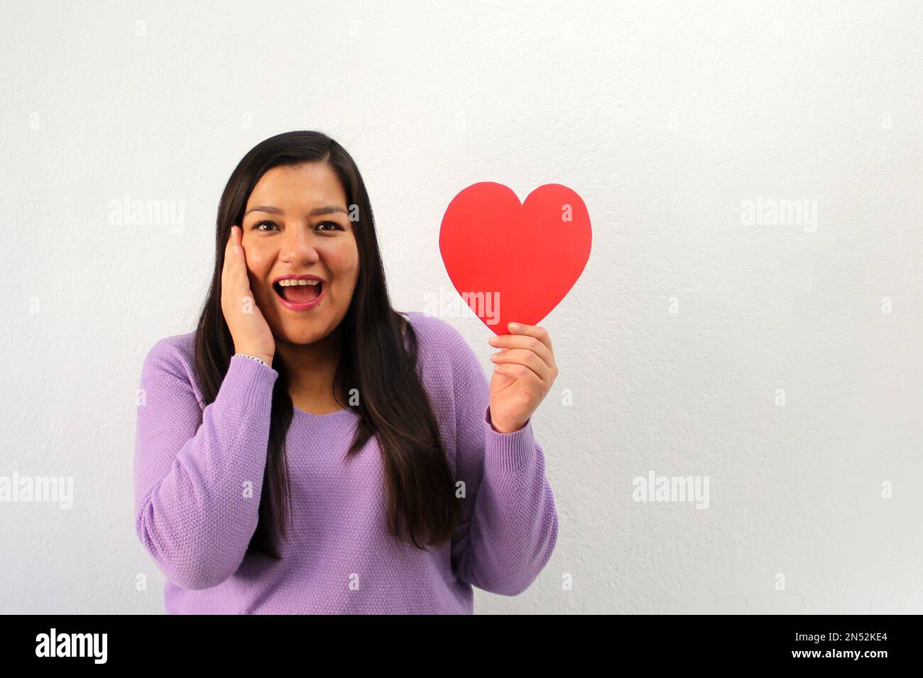 Latin adult woman with lila sweater with a big red heart shows her ...