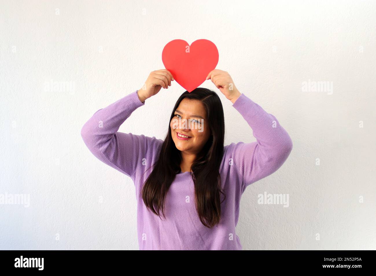 Latin adult woman with lila sweater with a big red heart shows her ...