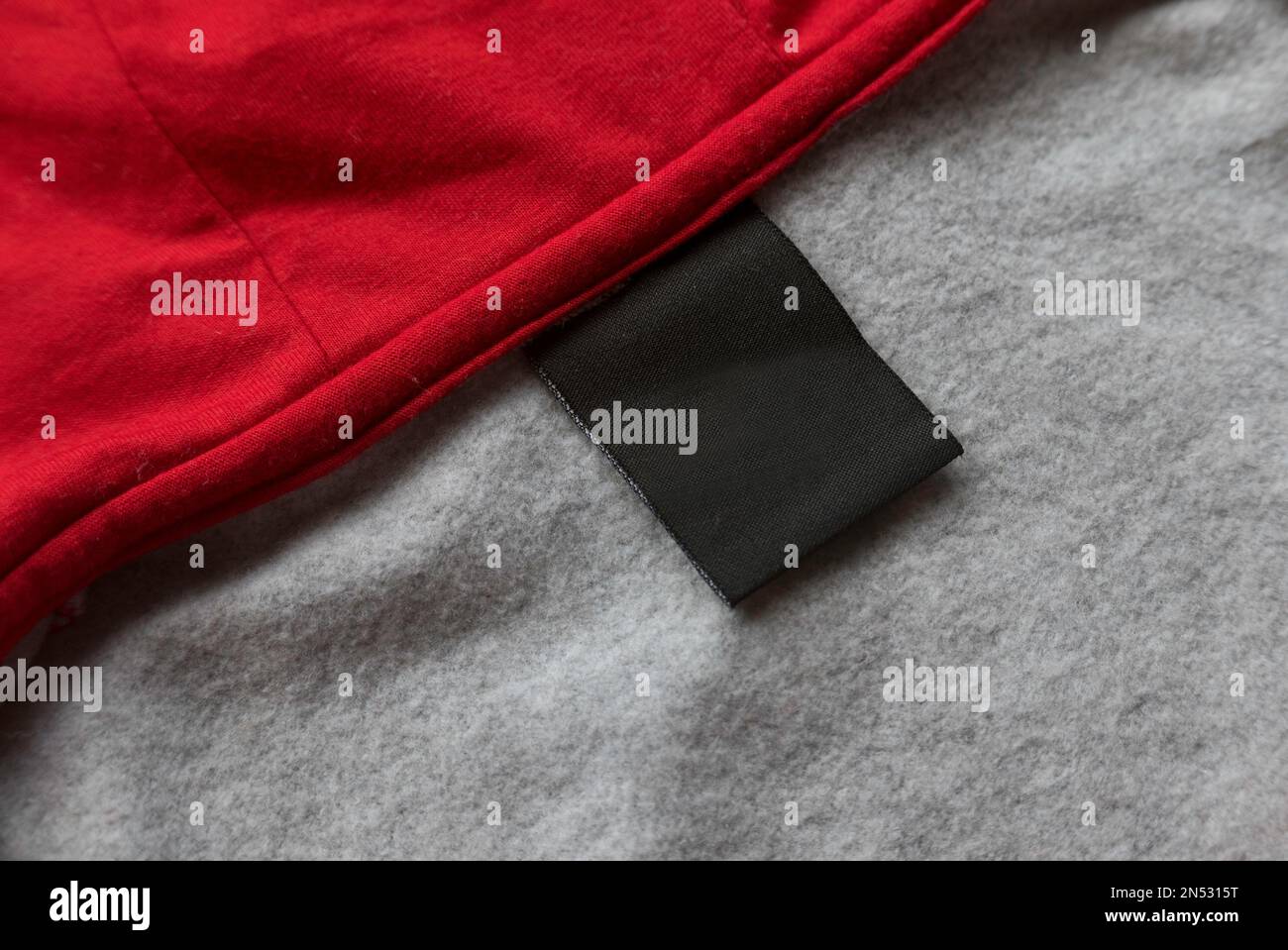 Blank black laundry care clothes label on red and grey fabric texture ...