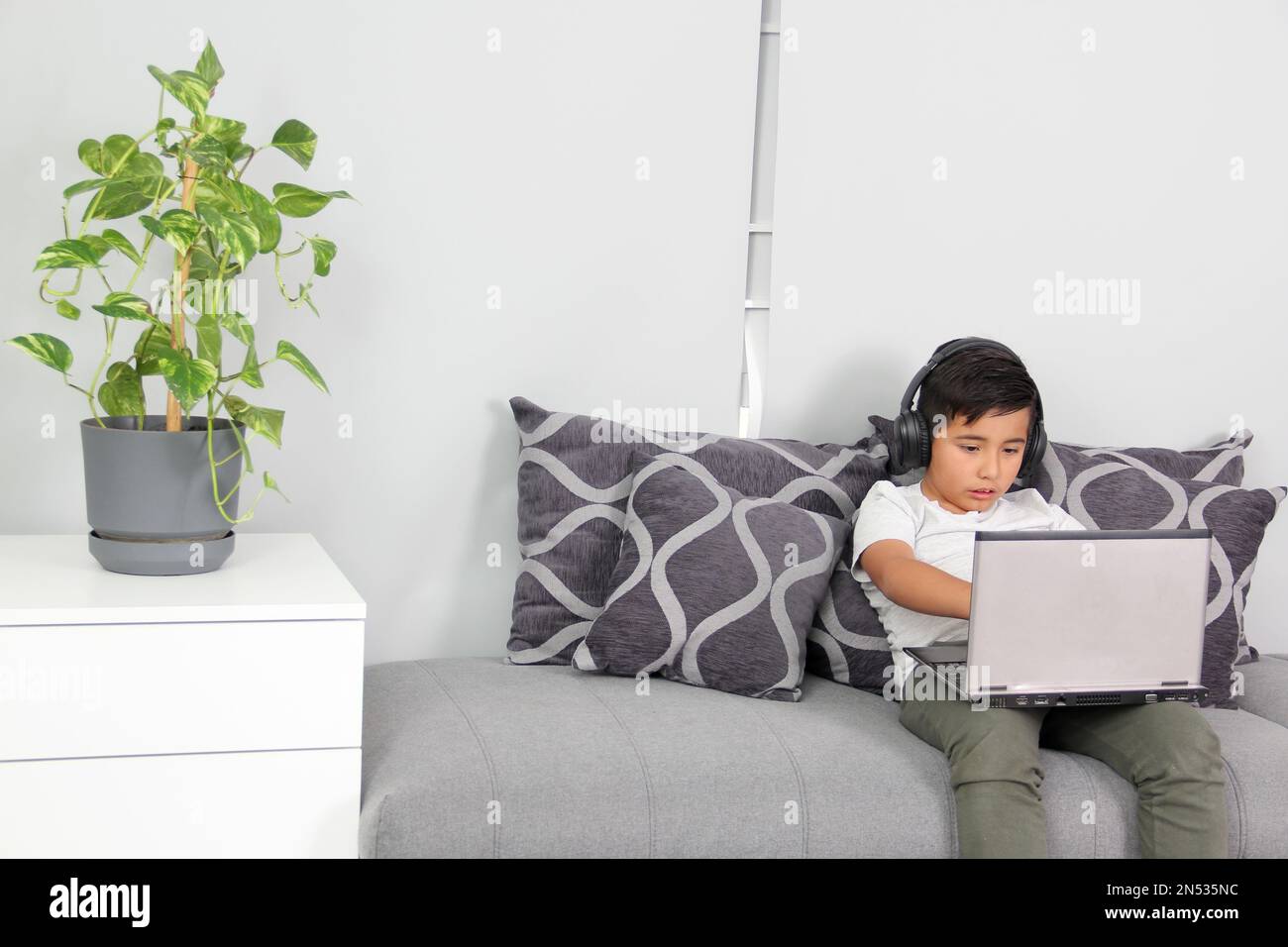 9-year-old Hispanic boy plays video games on his laptop with headphones ...