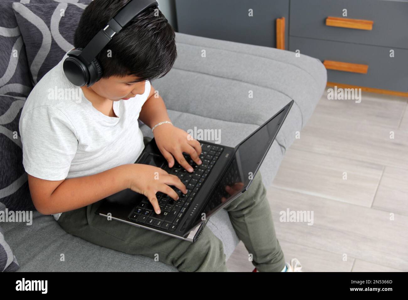 9-year-old Hispanic boy plays video games on his laptop with headphones ...