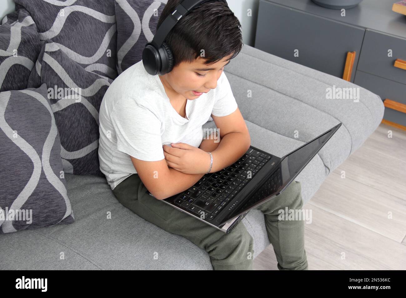 9-year-old Hispanic boy plays video games on his laptop with headphones ...