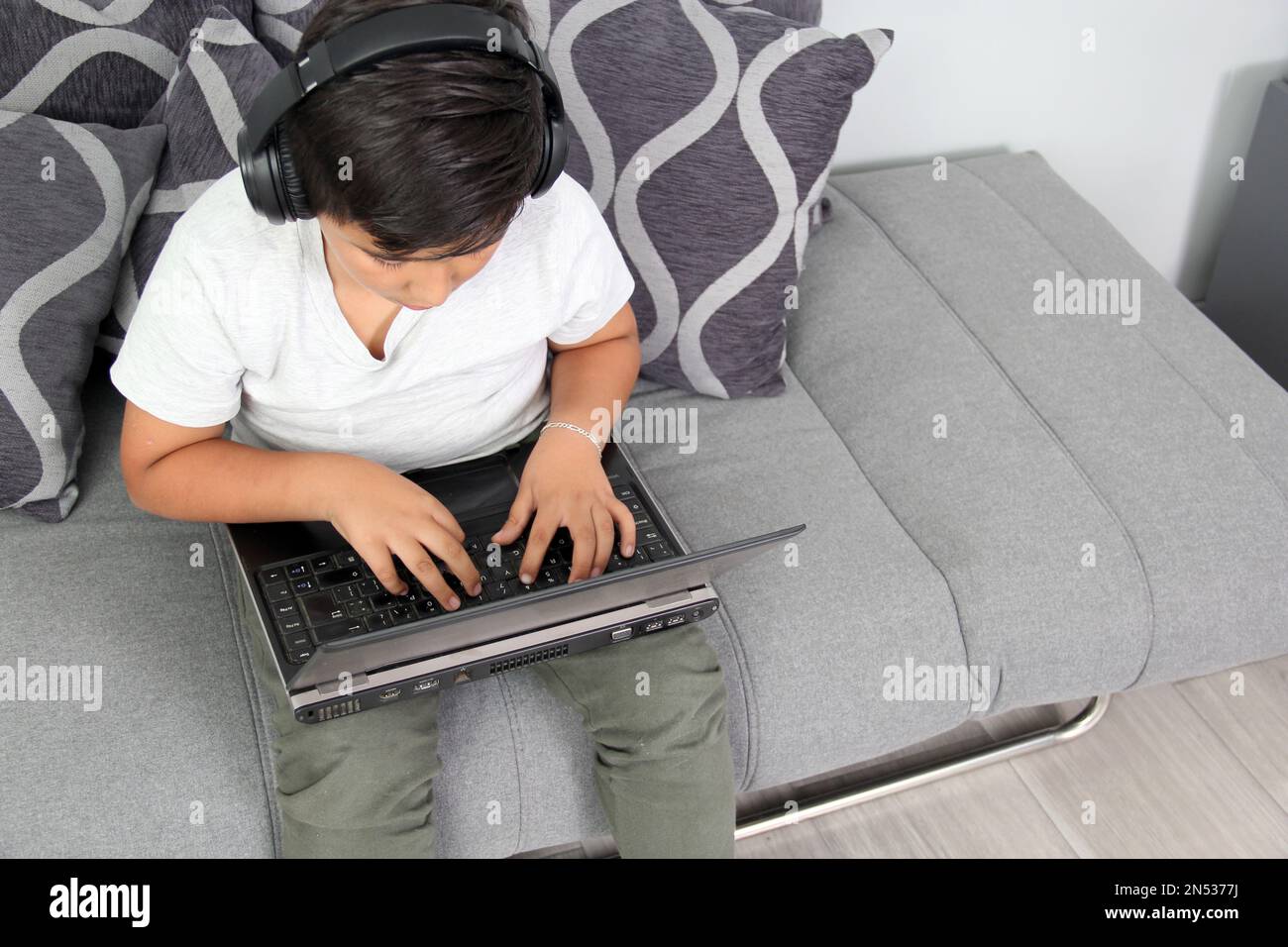 9-year-old Hispanic boy plays video games on his laptop with headphones ...