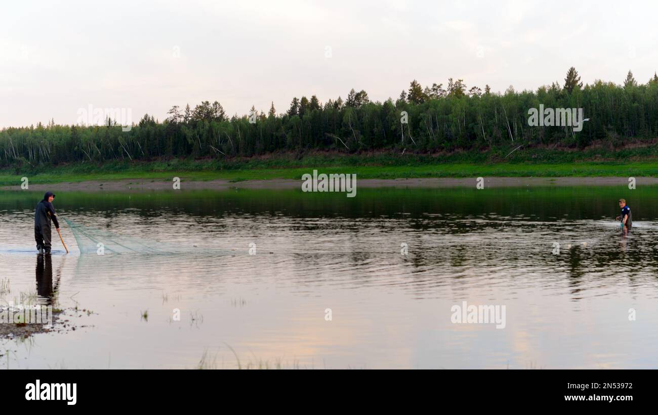 Two Yakut men turn around walking in waders with a fishing net along ...